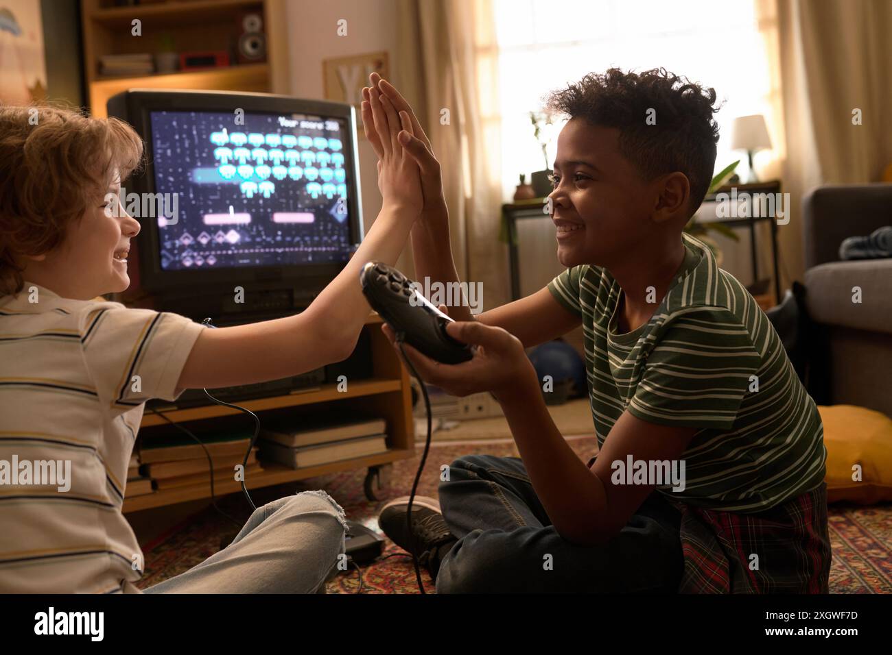 Pair of multiethnic kids high-fiving and celebrating a gaming victory ...