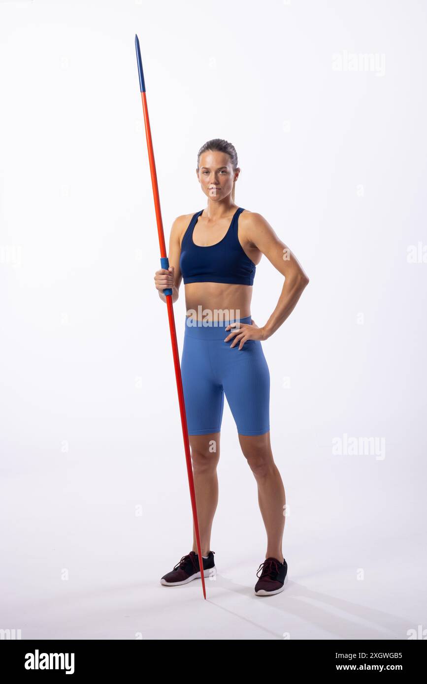 Athletic young Caucasian female athlete poses with a javelin on a white ...