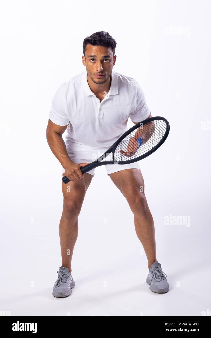 Young biracial man poses with a tennis racket on a white background ...