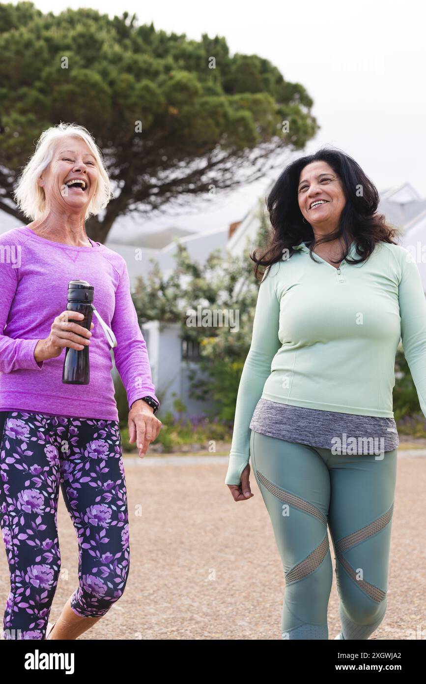 Two happy diverse senior female friends walking for exercise in country ...