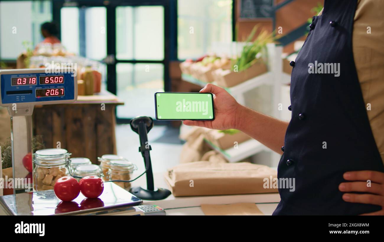 Merchant with phone greenscreen at store counter, presenting isolated ...