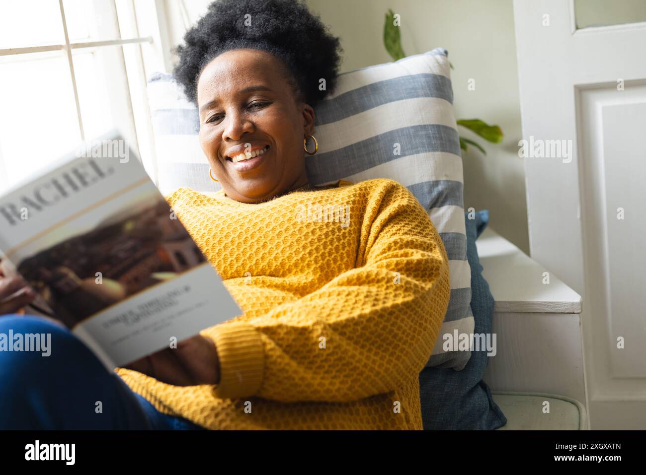 Happy senior african american woman lying on couch and reading book at ...