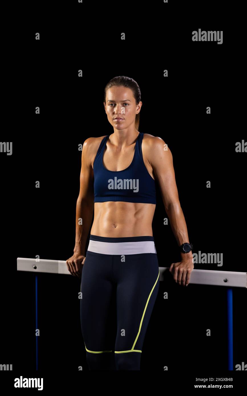Young Caucasian female athlete stands confidently at the gym on a black ...