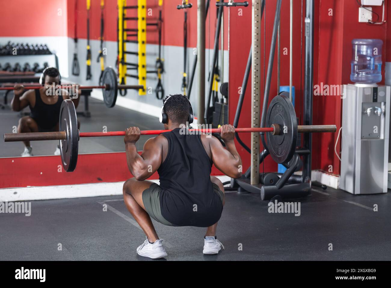 A fit African American man performs a squat at the gym. His focus on ...