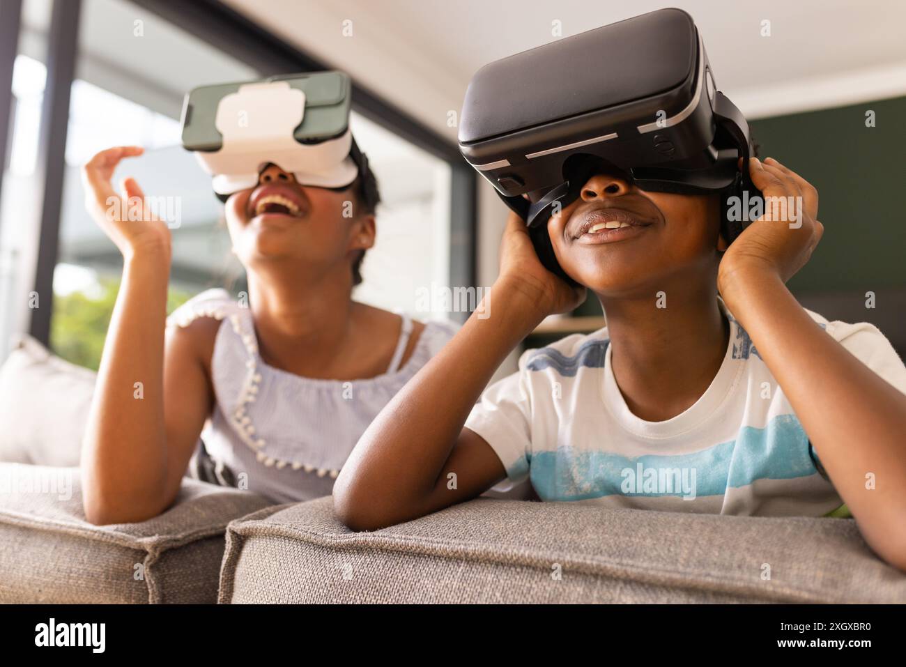 Teenage biracial brother and sister enjoy VR headsets at home. They're ...