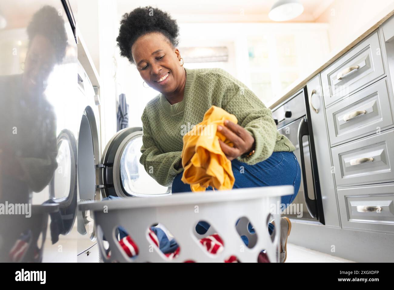 Happy senior african american woman doing laundry in kitchen at home ...
