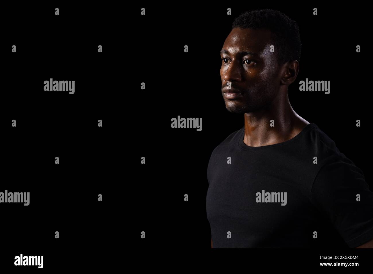African American man in a black shirt poses thoughtfully on a black background. His serious ...