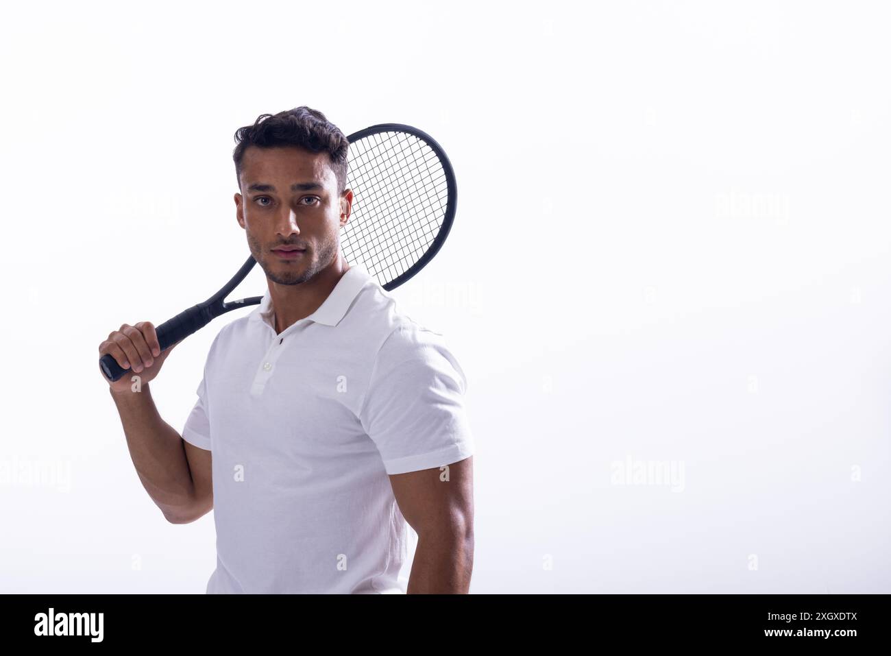 Young biracial man poses with a tennis racket on a white background ...