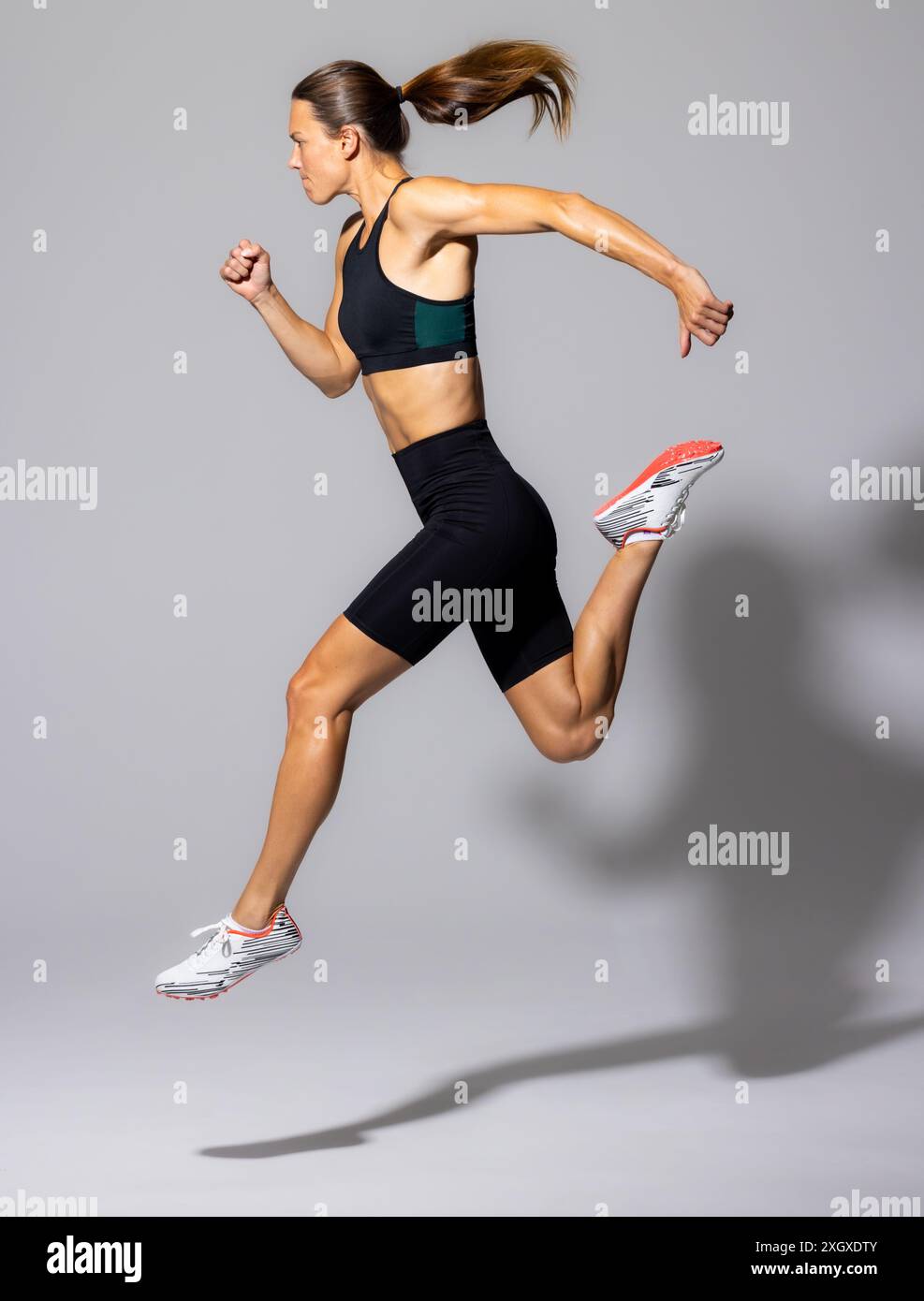 Athletic young Caucasian female athlete in mid-stride on a white background. She showcases ...