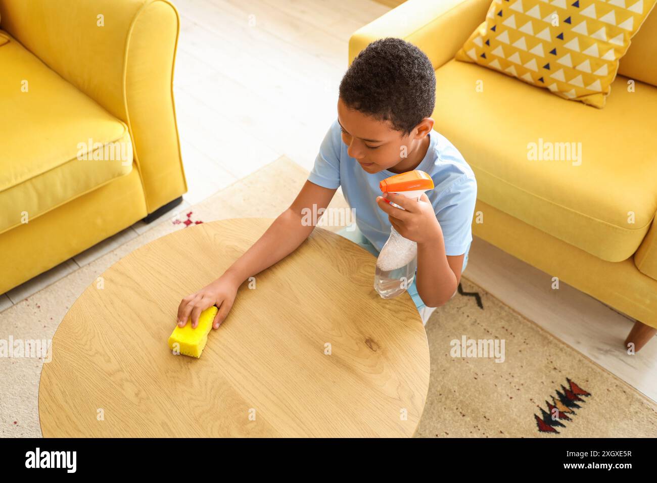 Cute little African-American boy cleaning table with sponge in living room Stock Photo - Alamy