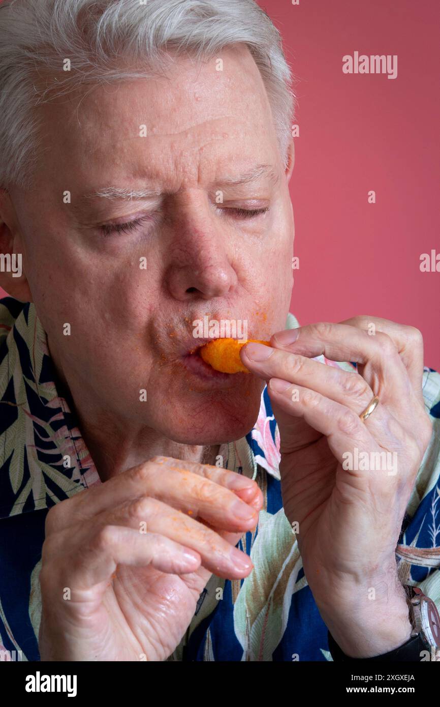 Senior man snacking on Cheetos and making a mess, 2024, USA Stock Photo ...