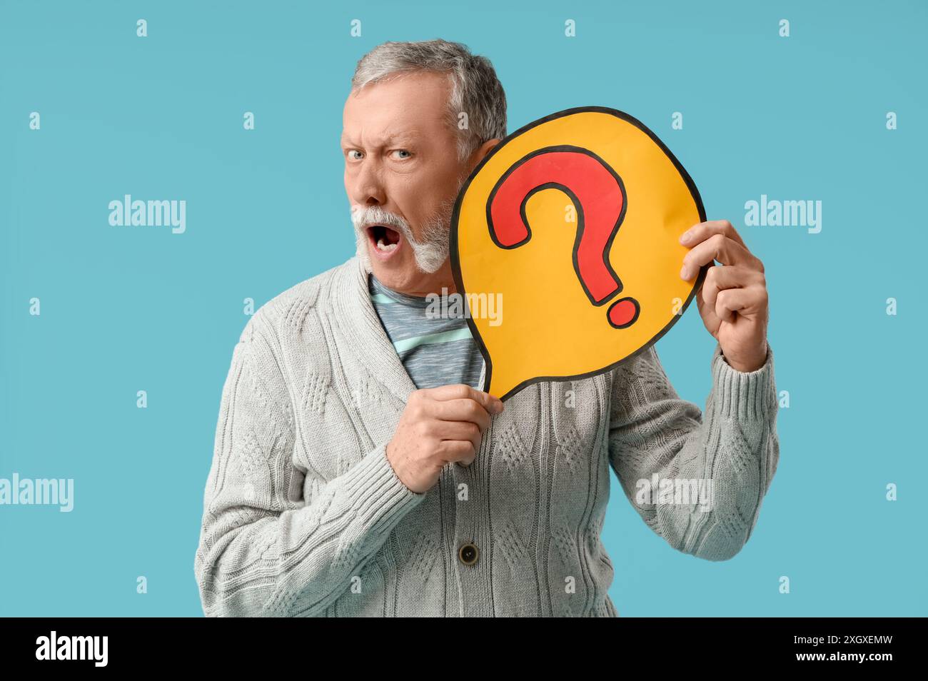 Shocked senior man holding speech bubble with question mark on blue ...