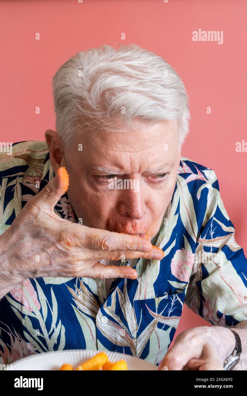 Senior man snacking on Cheetos and making a mess, 2024, USA Stock Photo ...