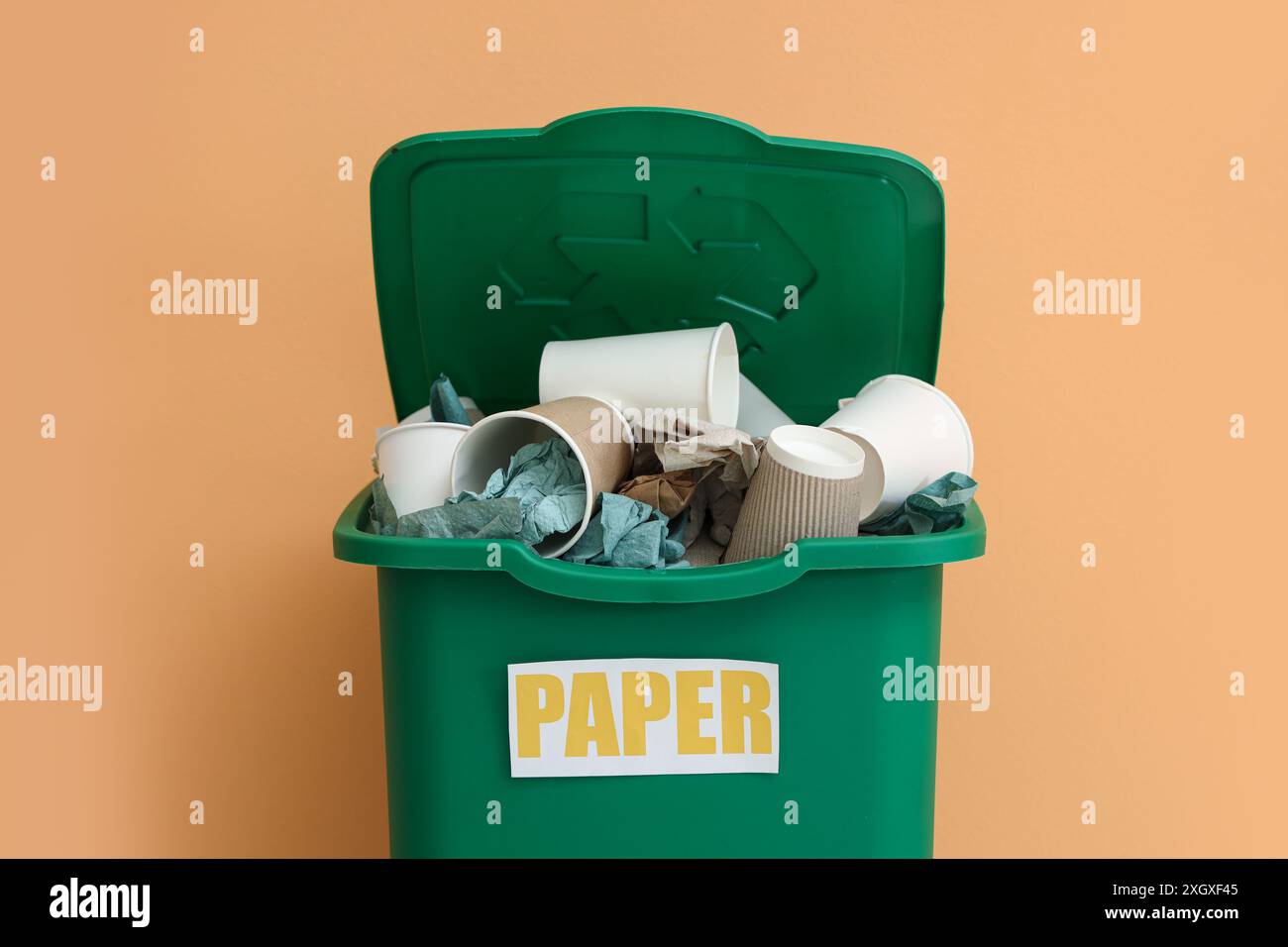 Green recycling bin with paper litter near beige wall. Recycle concept ...