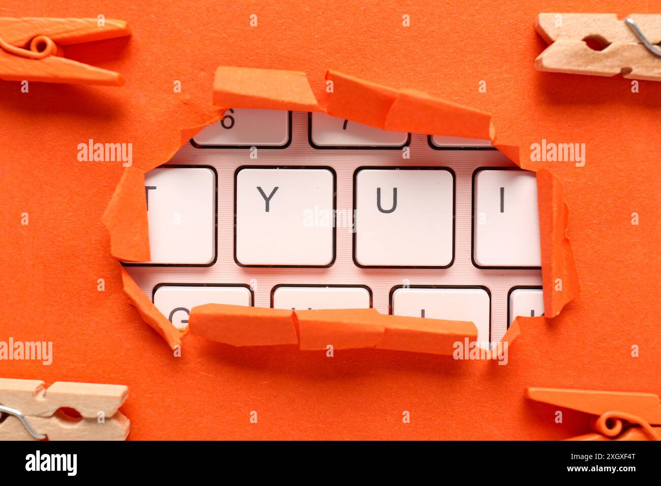 Computer keyboard visible through torn paper and clothespins on orange ...