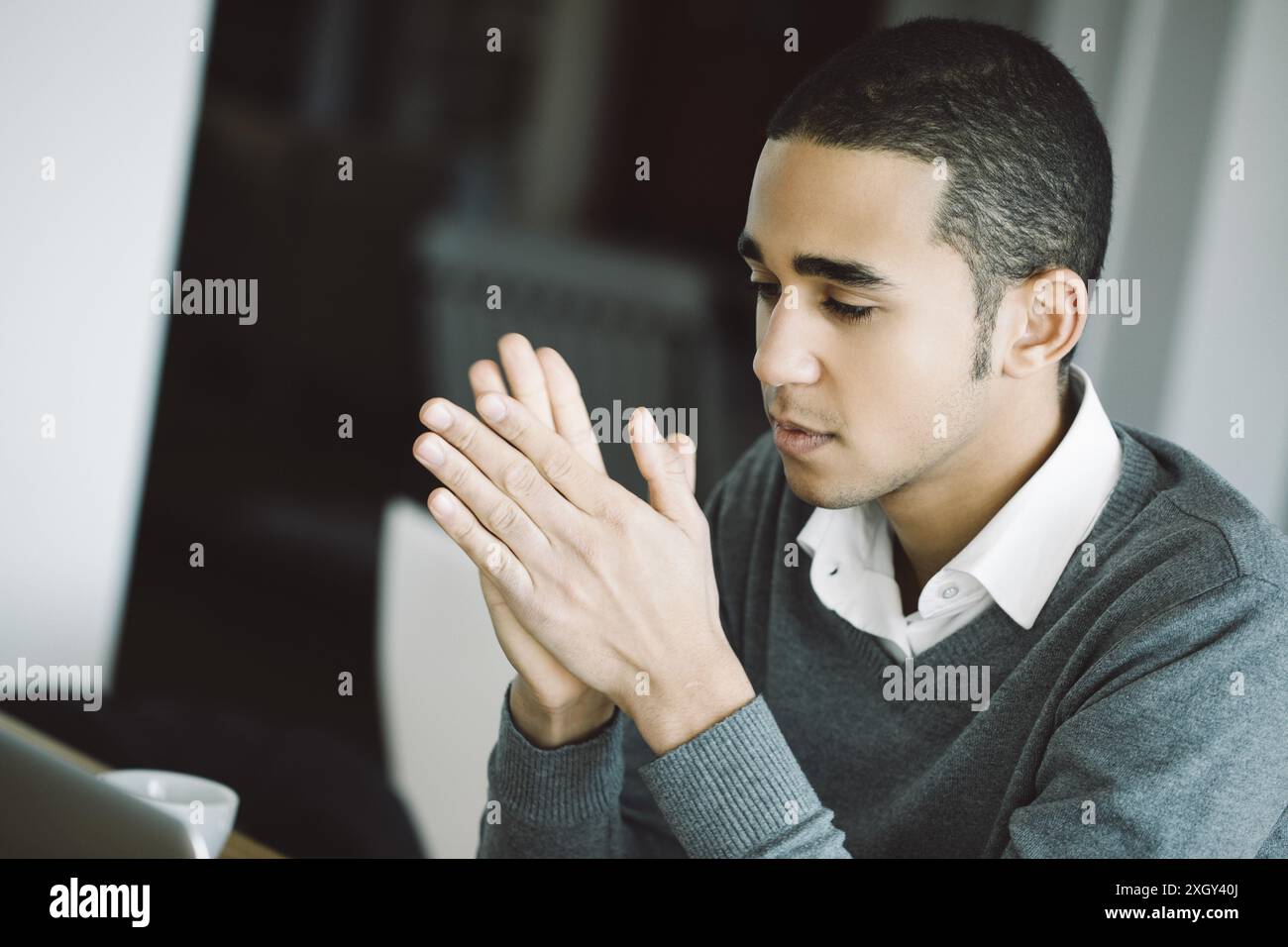 Young man in a gray sweater and white shirt rubs his hands together ...