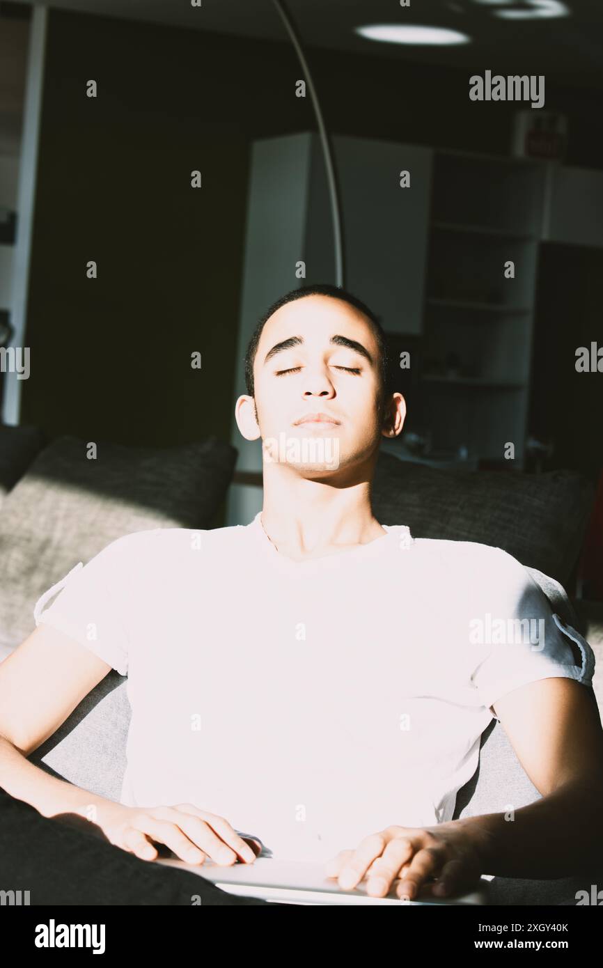 Young man in a white t-shirt sits with eyes closed, basking in the ...
