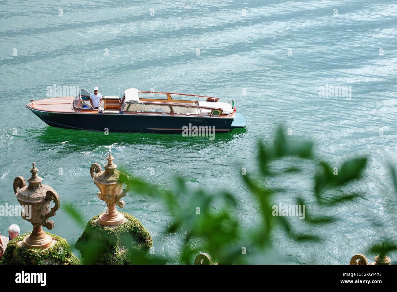 A classic wooden speedboat waits with its driver on the turquoise lake ...