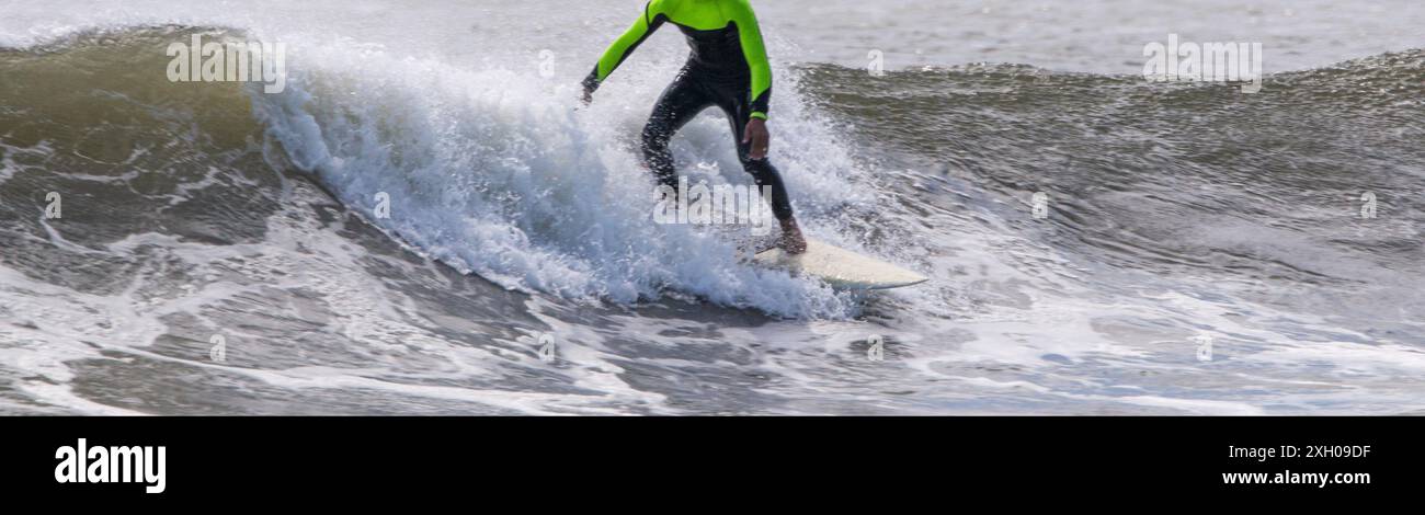 Horizontal view of a Boy surfing on a breaking wave wearing a black and ...