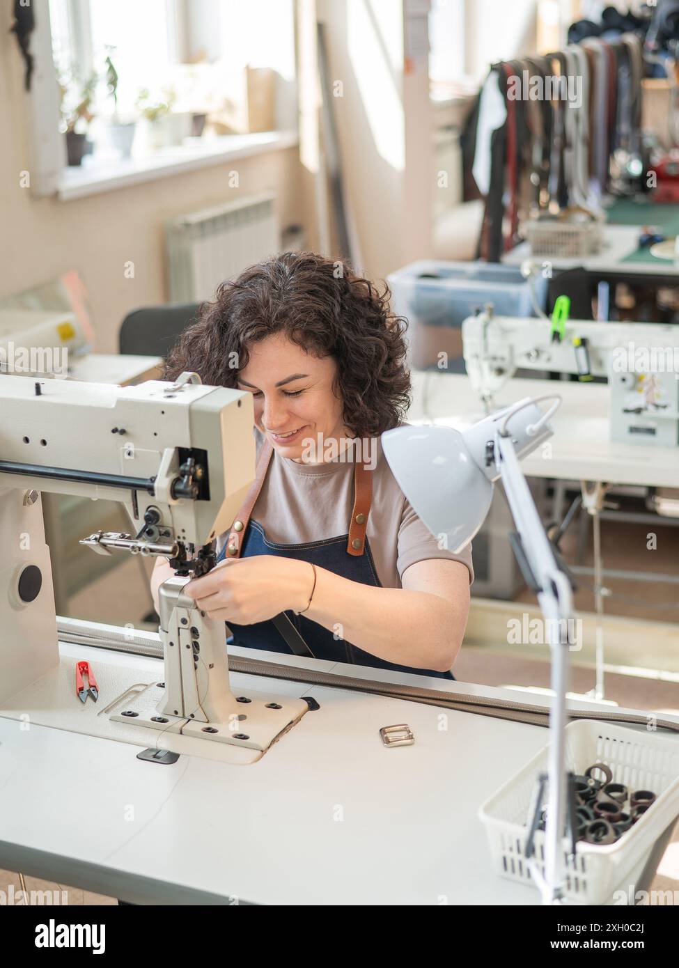 A woman tanner sews a leather belt on a sewing machine. Vertical photo ...