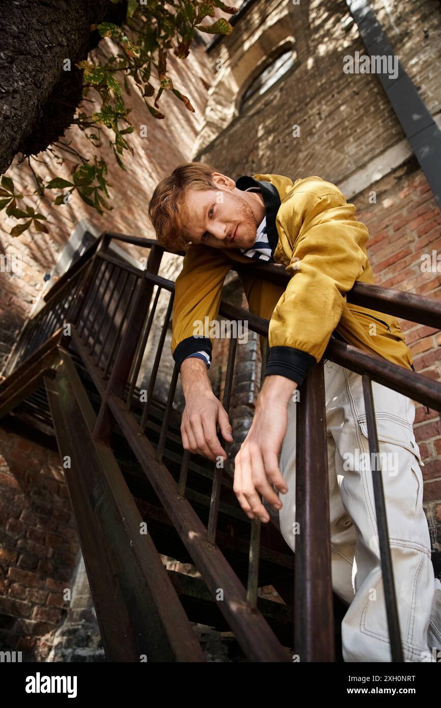 A stylish red-haired man in debonair attire leans on a rail next to a ...