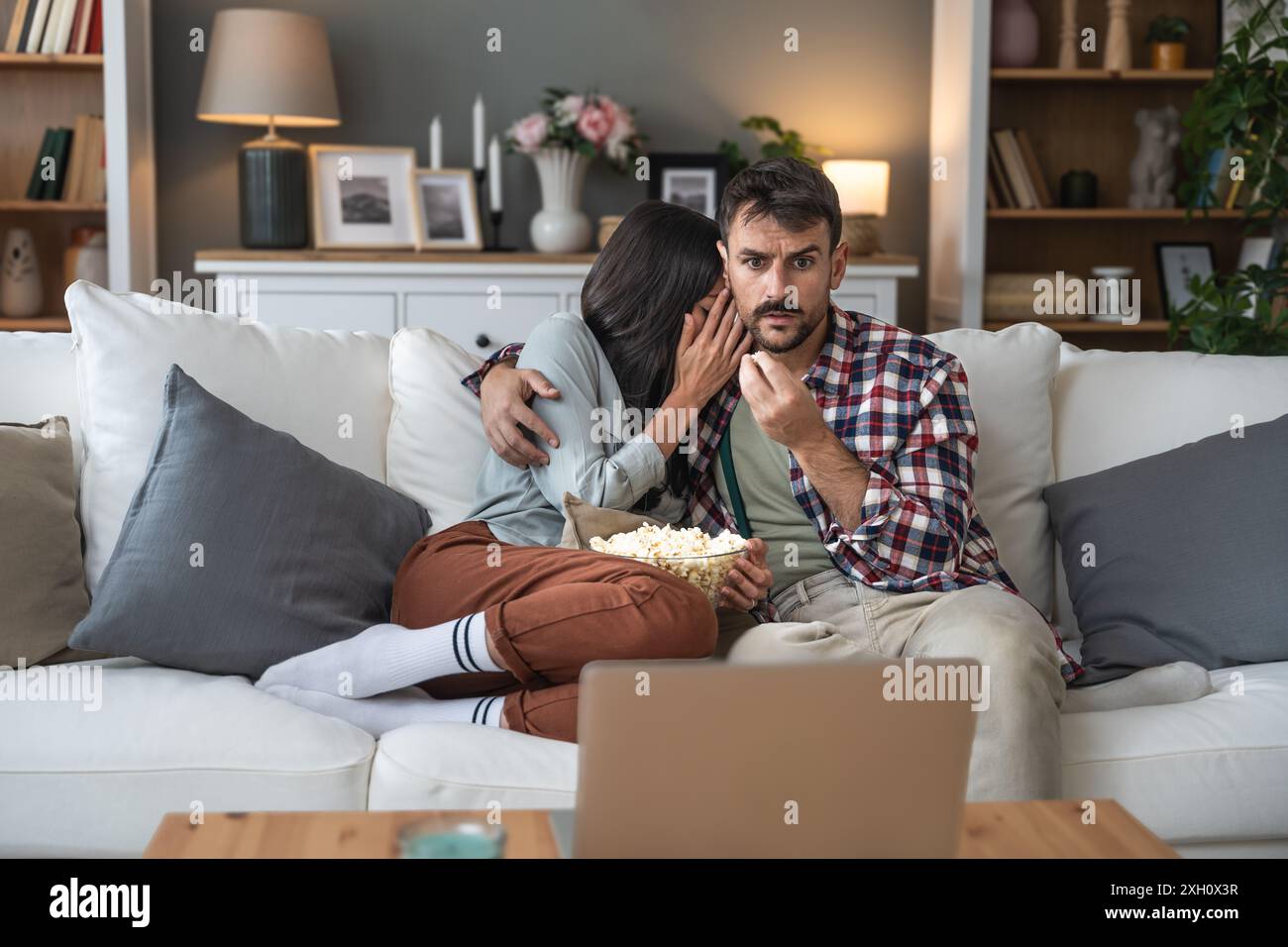 Couple shocked watching horror movie on laptop computer sitting at sofa ...