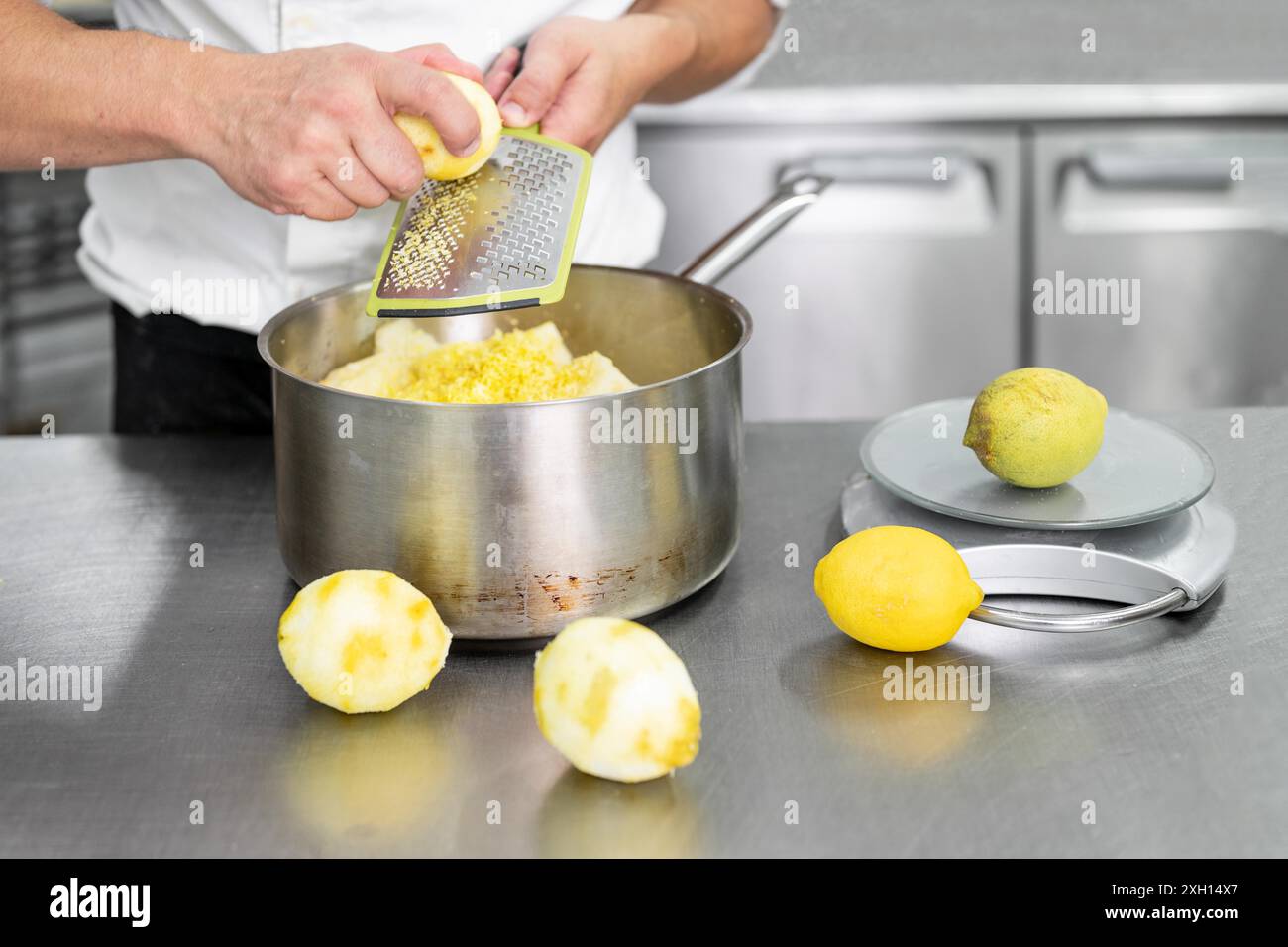 A Pastry chef's hand grates lemon in commercial kitchen. Chef grates ...