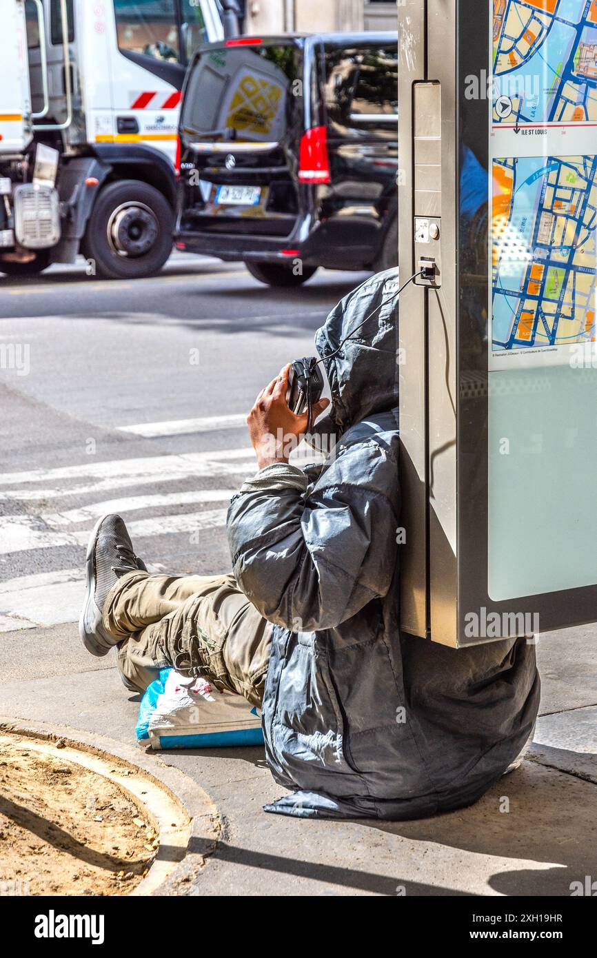 Homeless man sat on pavement with phone plugged into bus-stop outlet ...