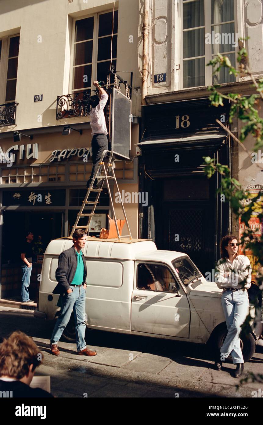 Street scene in Paris: a man installing a restaurant sign climbed on ...