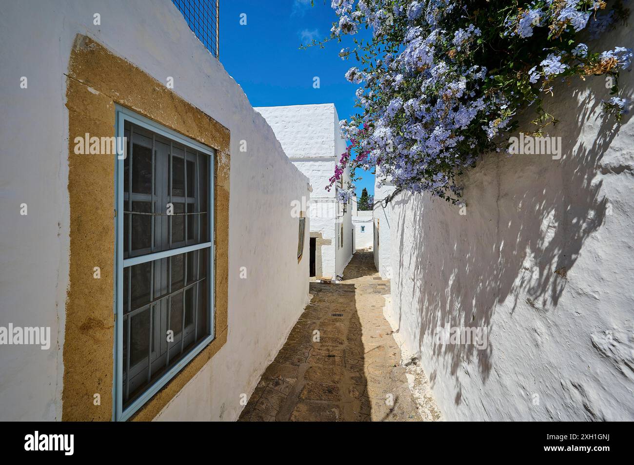 Narrow street with white walls, a window and blooming flowers under a ...