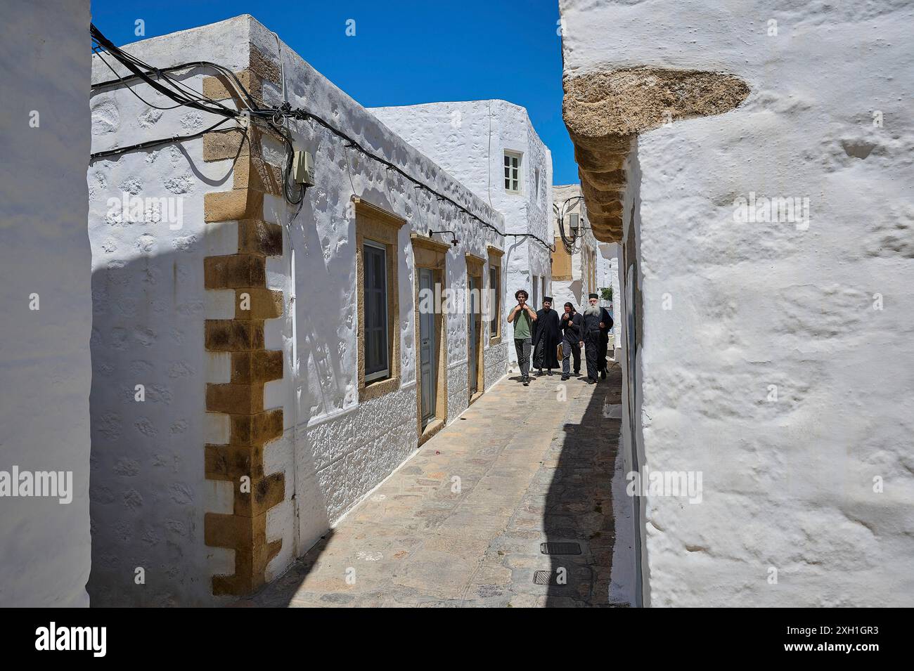 Sunny narrow alley with white buildings and a group of people ...