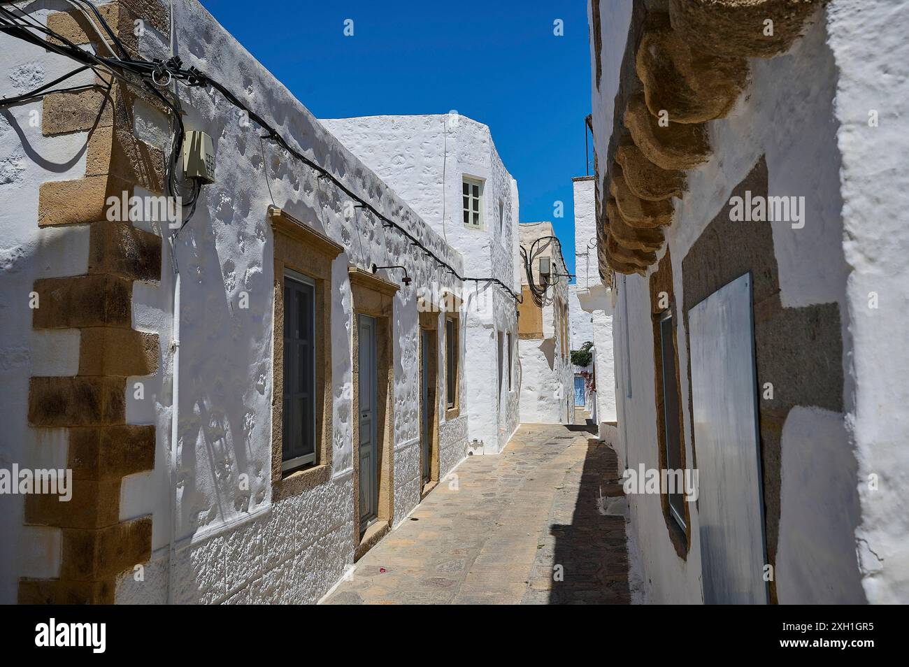 Narrow alley between white, historic buildings under a clear blue sky ...