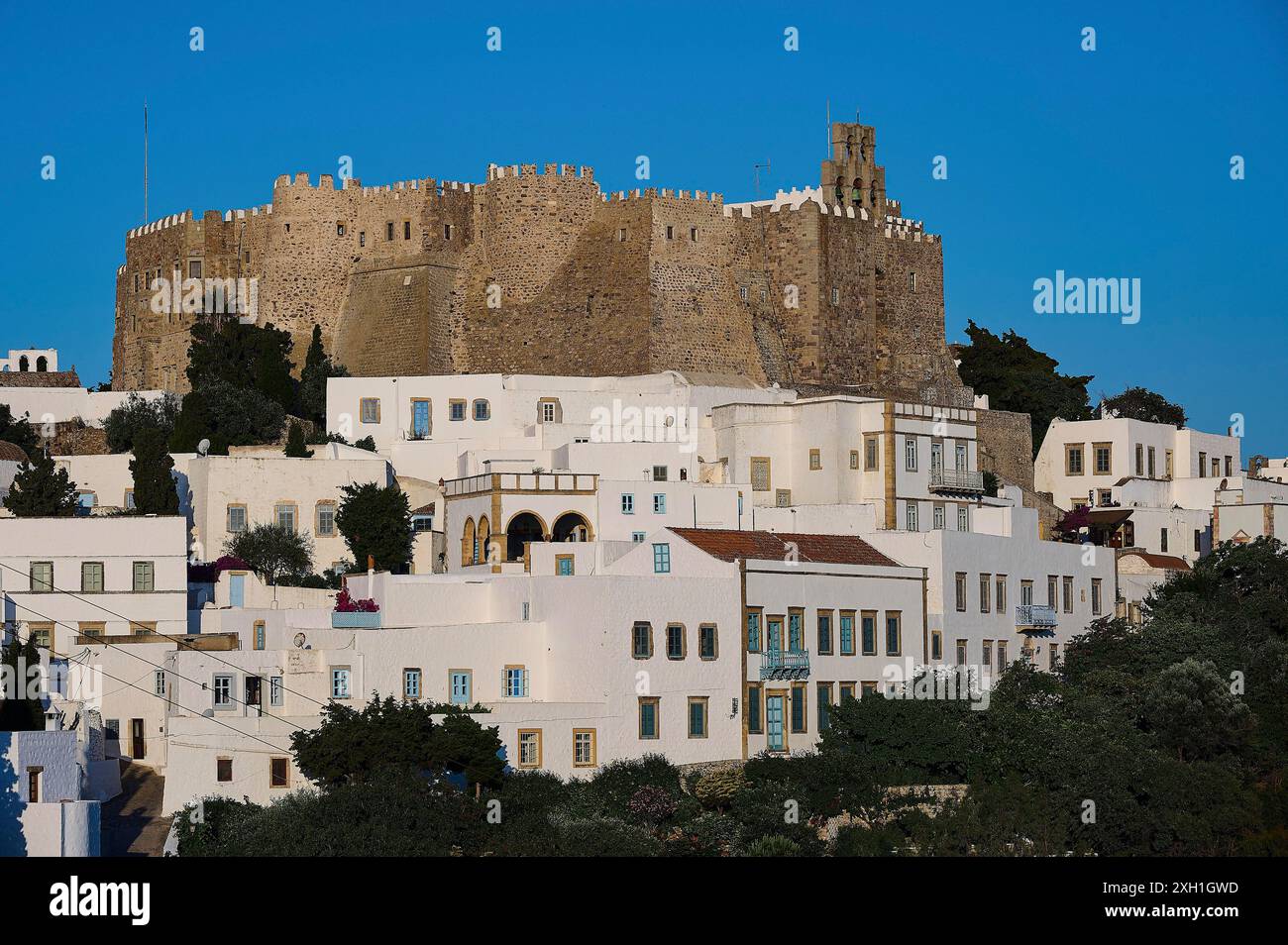 Old castle above a whitewashed village, surrounded by cypresses and ...