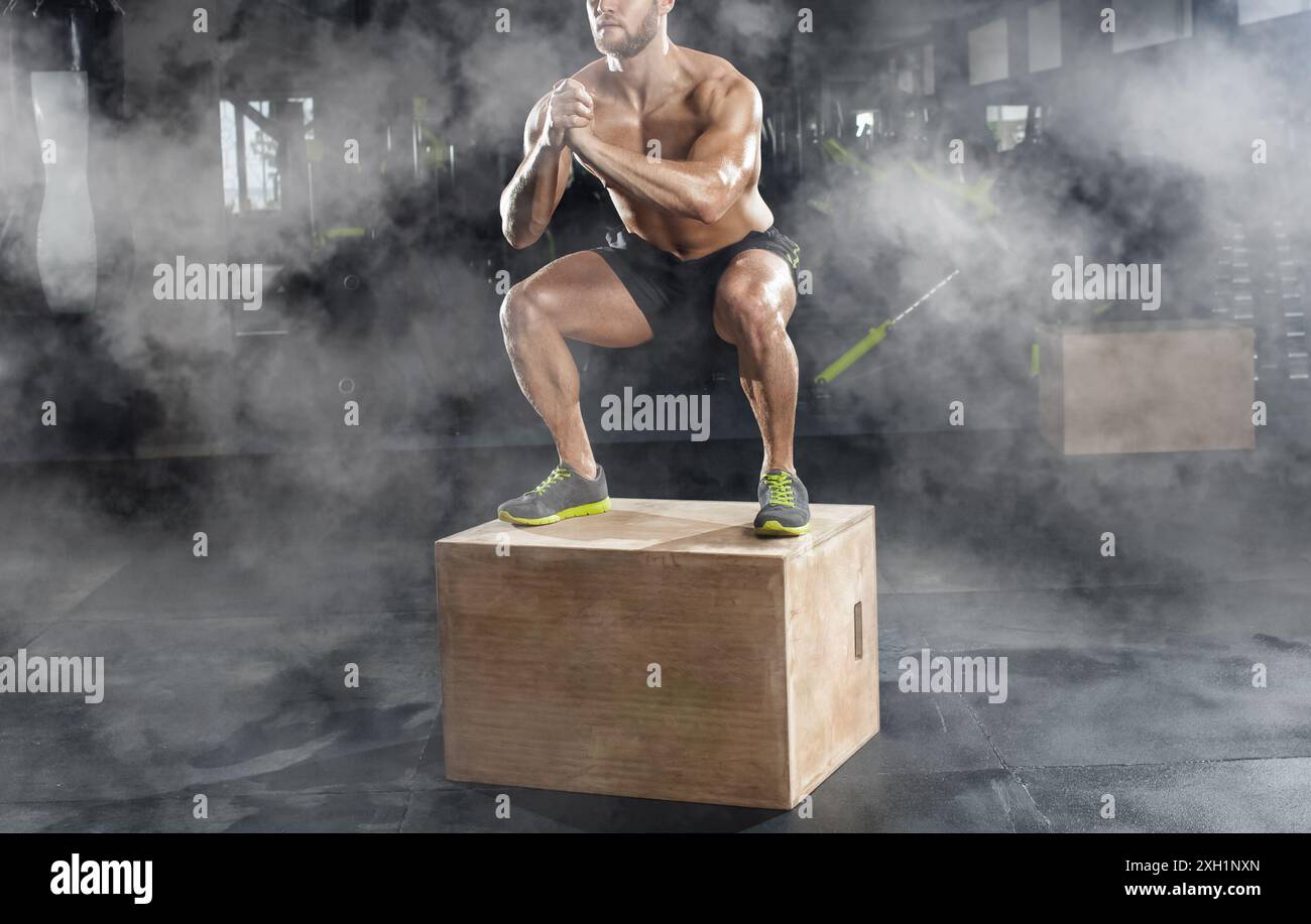 Bodybuilder man, does the cardio exercise, jumping on a wooden box in ...