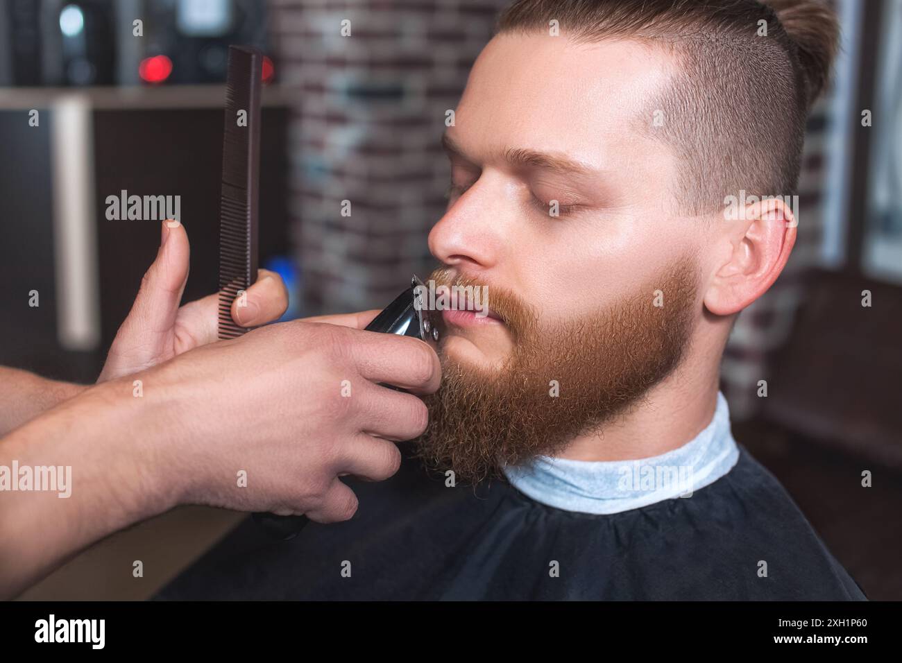 A male barber at work, he does a beard and mustache haircut to a man in ...