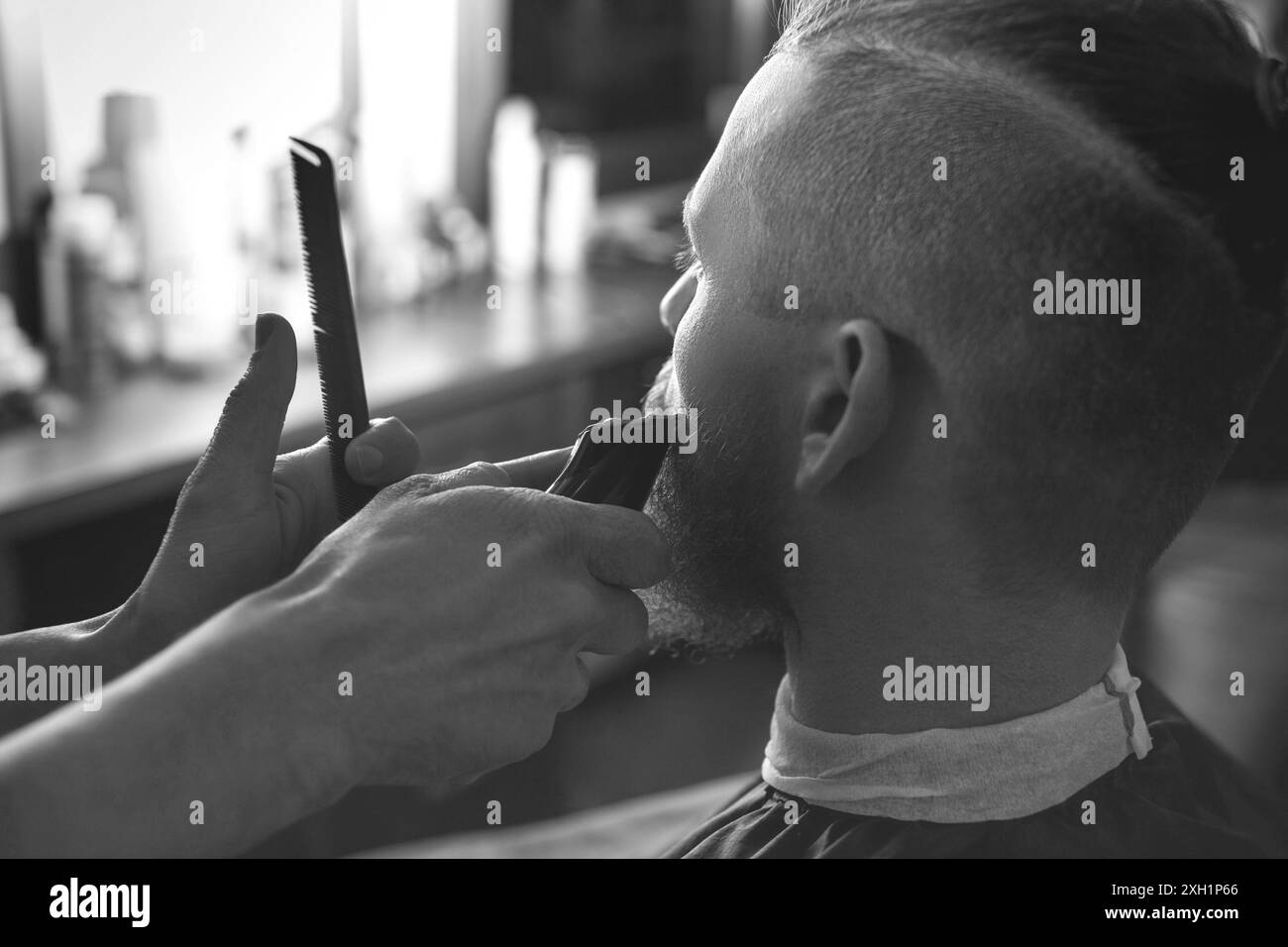 A male barber at work, he does a beard and mustache haircut to a man in ...