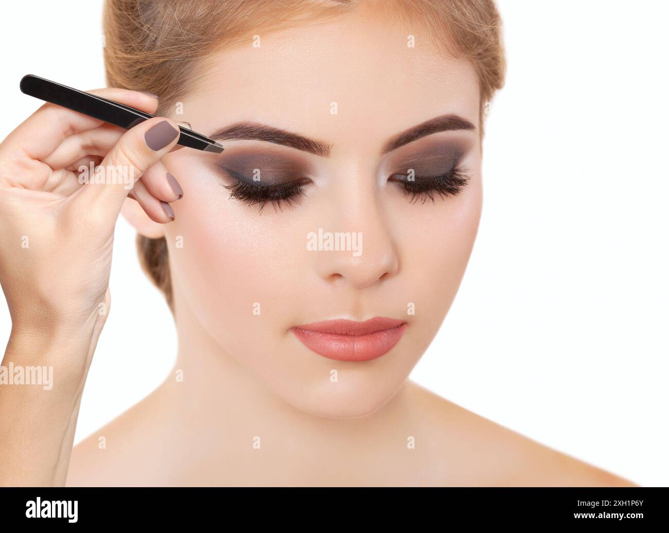 Make-up artist plucks eyebrows with tweezers to a woman with smoky eyes makeup. Beautiful thick ...