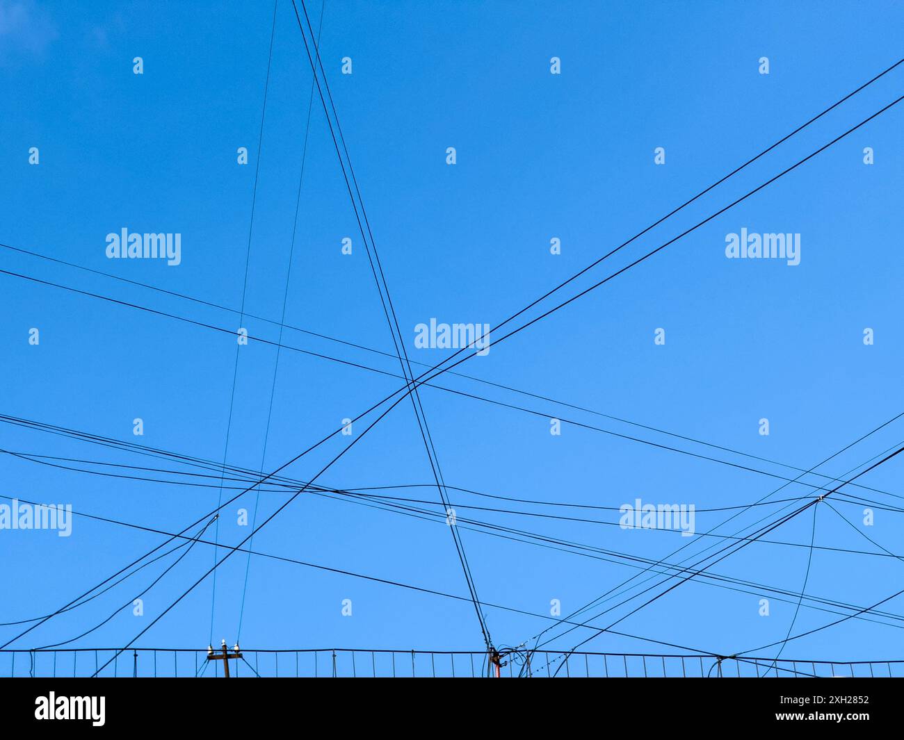 Tangled power lines intersect against a bright blue sky, creating a ...