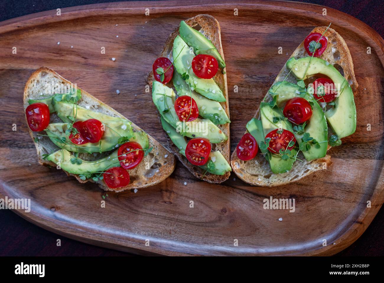 A slice of toasted sour dough bread with avocado and tomato on top ...