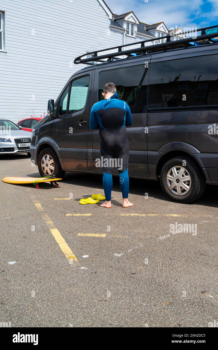 A surfer standing in a car park with his surfboard preparing to go ...