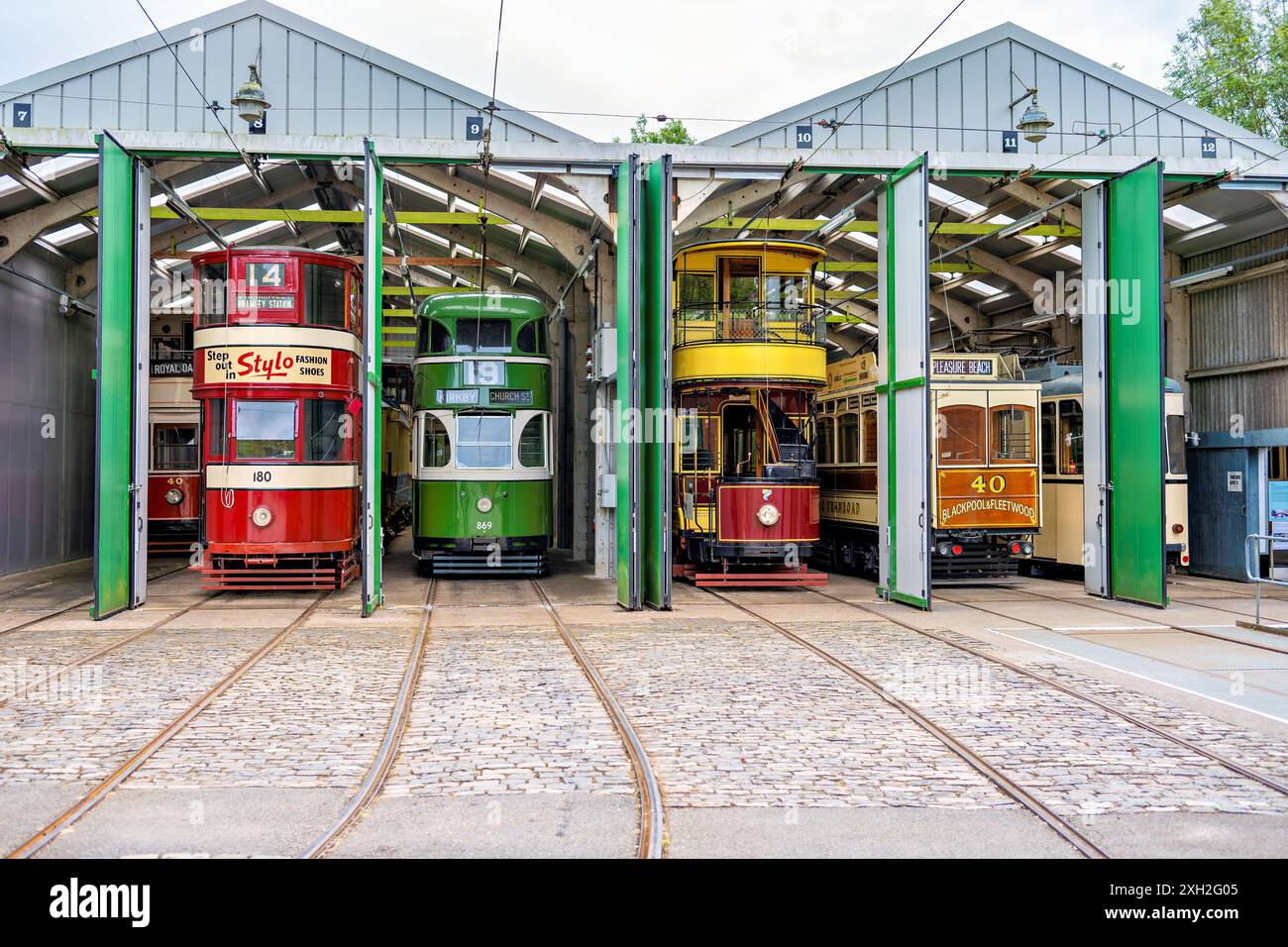Vintage trams lined up inside a historic tram shed with open doors ...