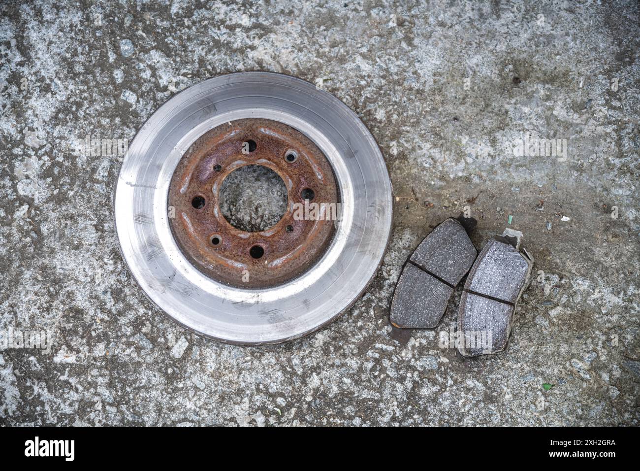 The old brake disc and brake pads are lying on a concrete surface ...
