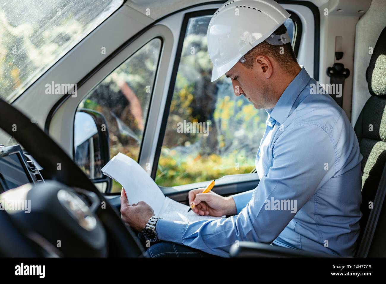 A construction worker wearing a white hard hat sits in the driver's ...