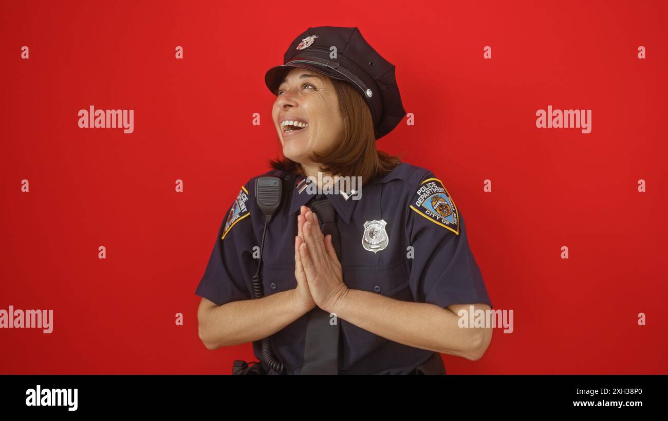 A joyful hispanic female police officer posing against a red background ...