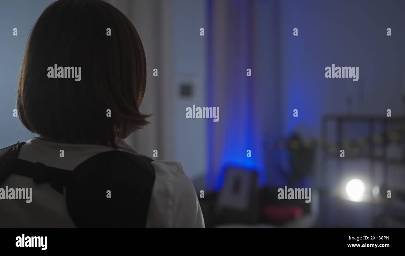 Back view of a mature woman in a dark office looking into a room with ...