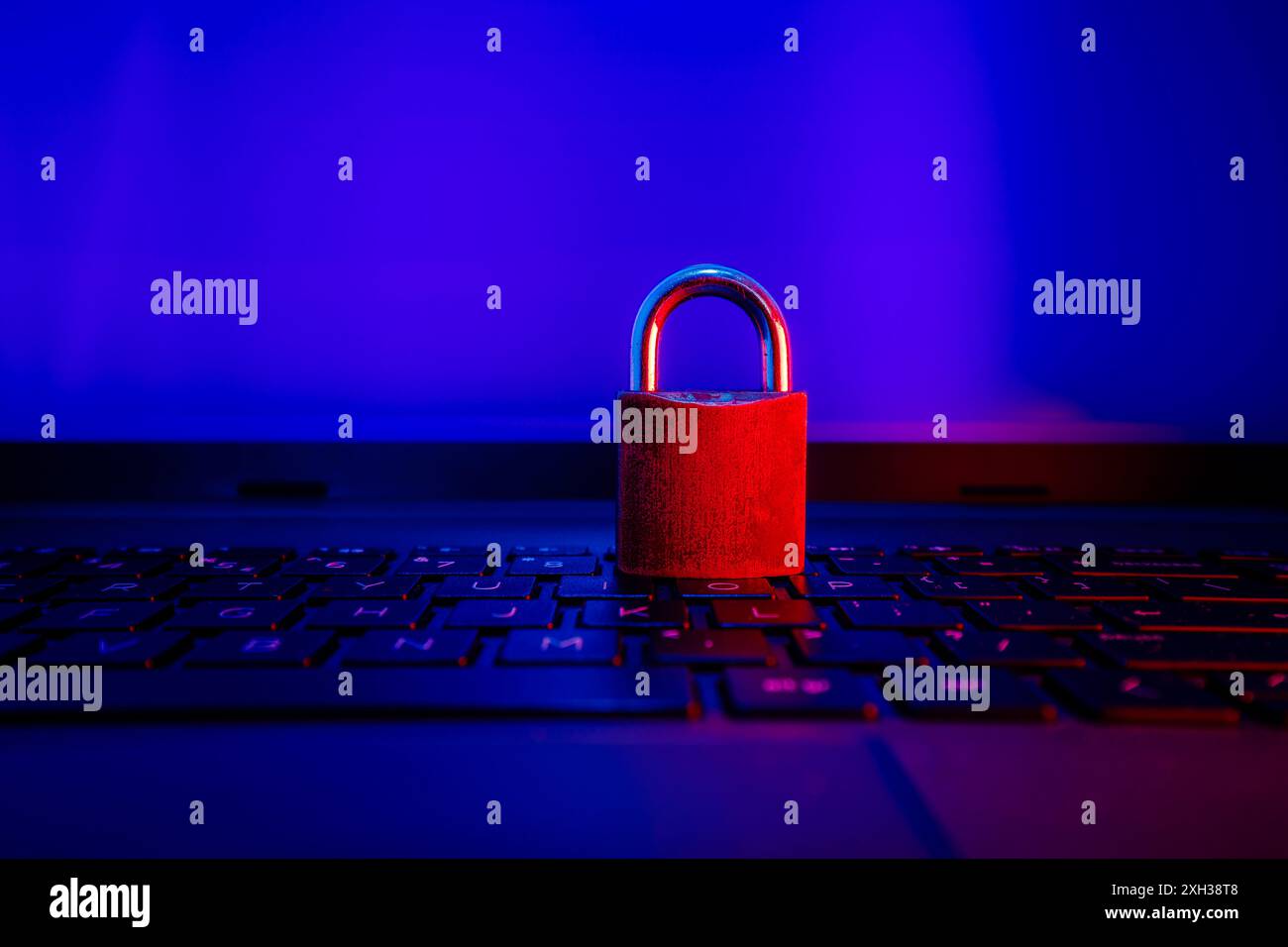 A red padlock sits on a laptop keyboard, illuminated by blue and red ...