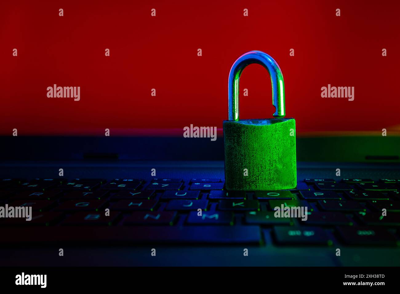 A metal padlock sits on a laptop keyboard, illuminated by red and blue ...
