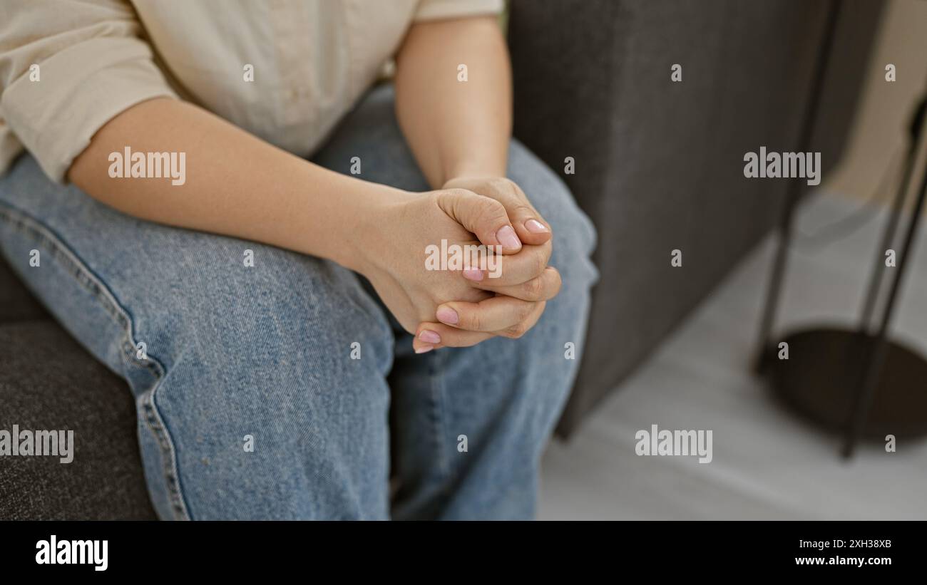 A close-up of a young woman’s folded hands resting on her lap in a ...