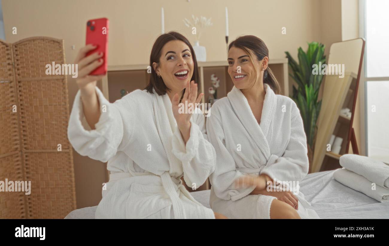 Two women wearing white robes take a selfie together in a spa ...