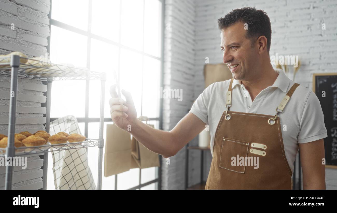 Man in bakery wearing an apron checking his phone indoors with shelves ...